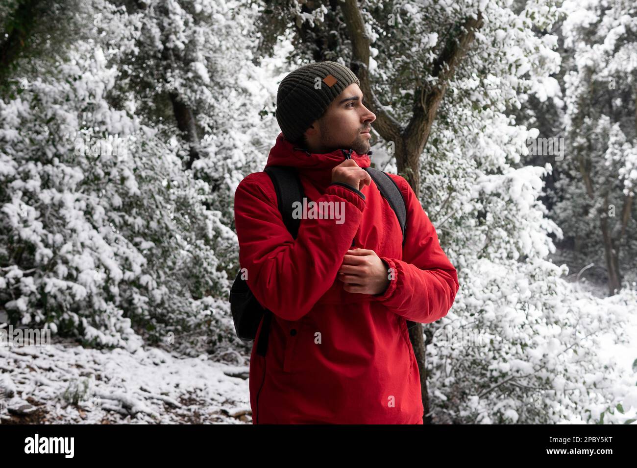 Young bearded male explorer in warm clothes and cap standing in winter ...