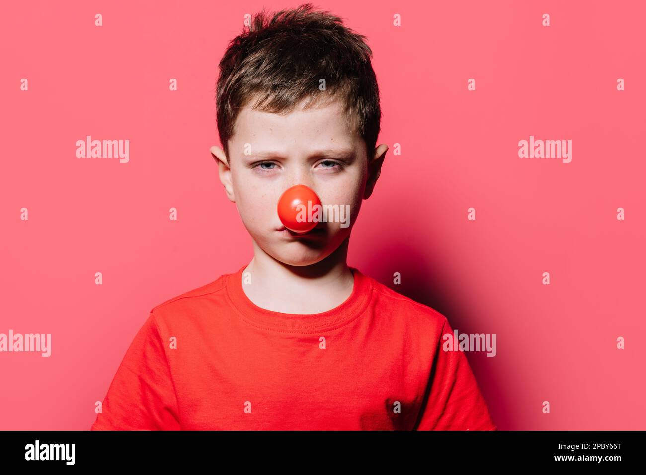 Portrait of young boy with angry face in red casual shirt and red nose ...