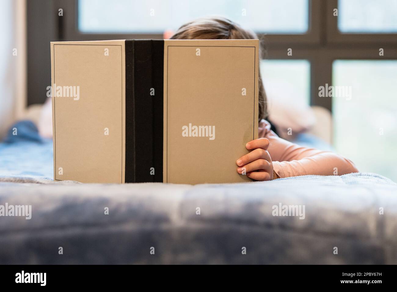Anonymous girl lying on soft single bed near window and hiding behind ...