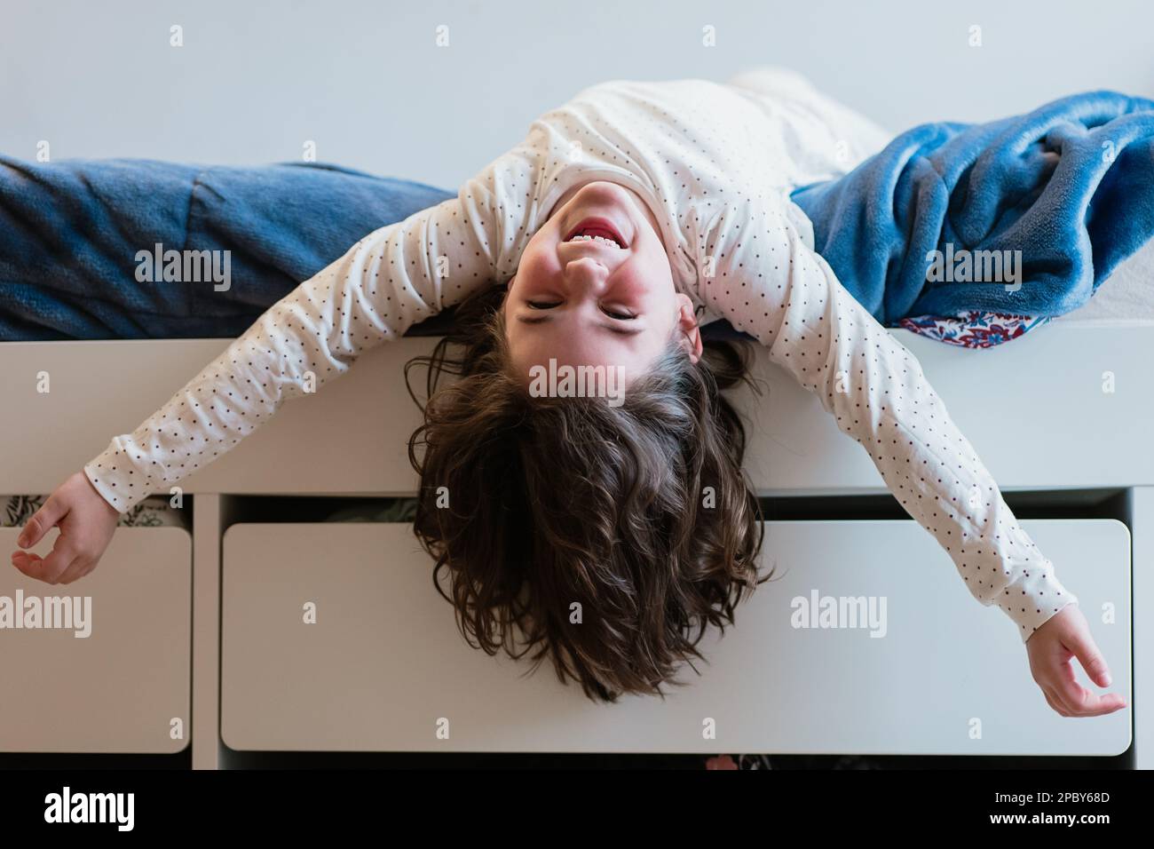Cheerful preteen girl with brown hair in pajama lying upside down with ...
