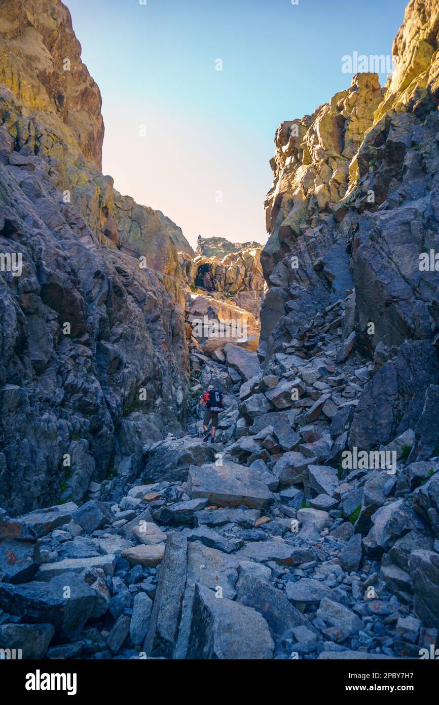 Tourist hiking on narrow stony path between rocky mountains on sunny ...
