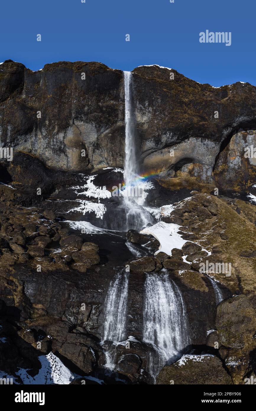 Breathtaking waterfall creating rainbow falling from rough rocky cliff ...