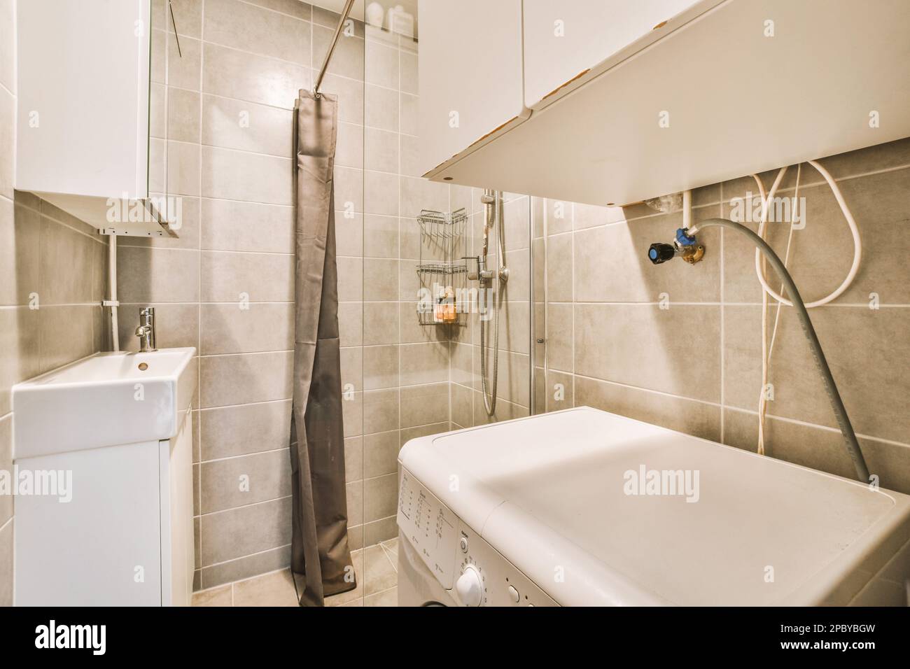 Shower cabin and washing machine placed against ceramic sink in modern ...