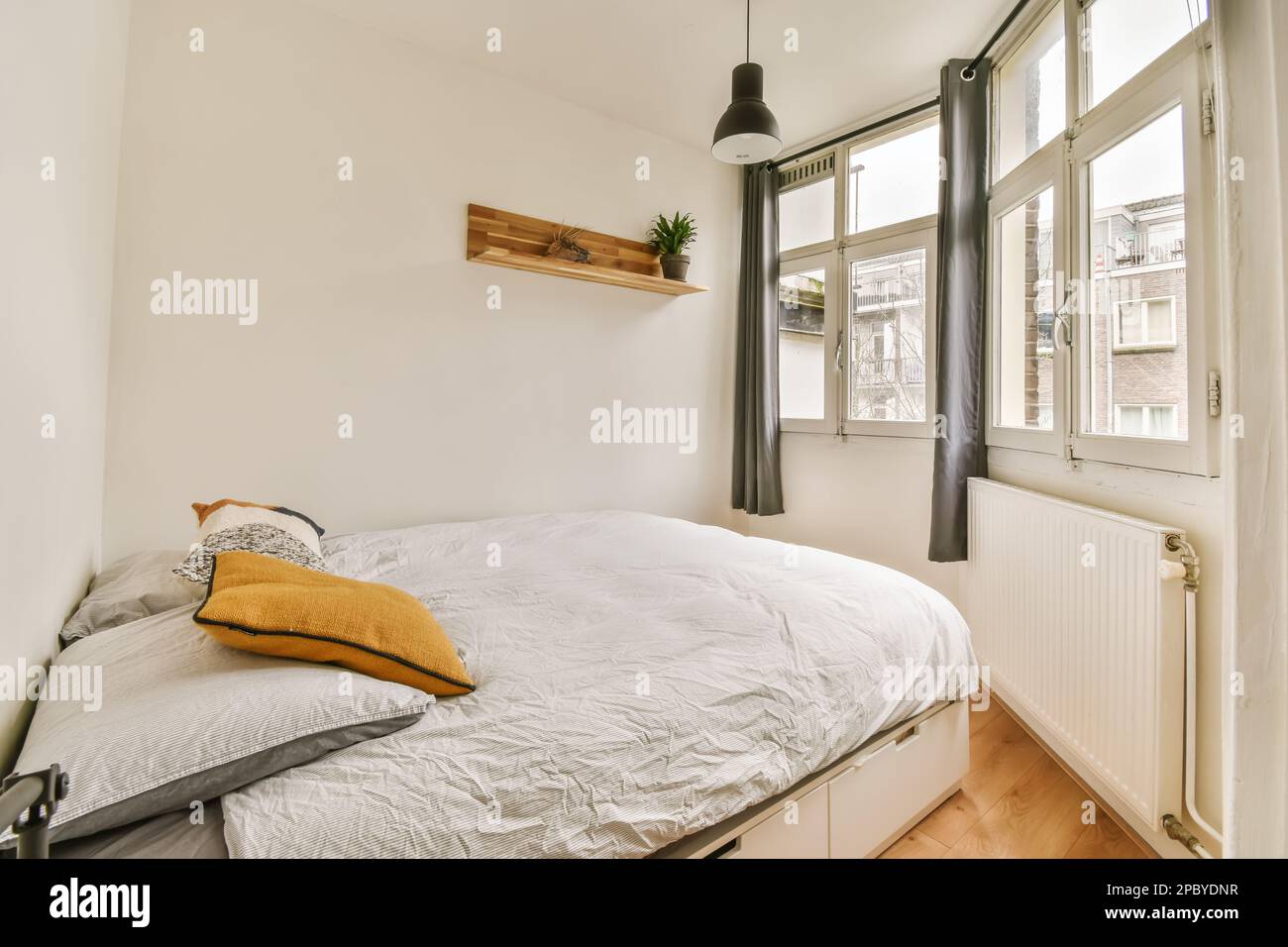 Comfortable bed with linen and cushions placed against windows with ...