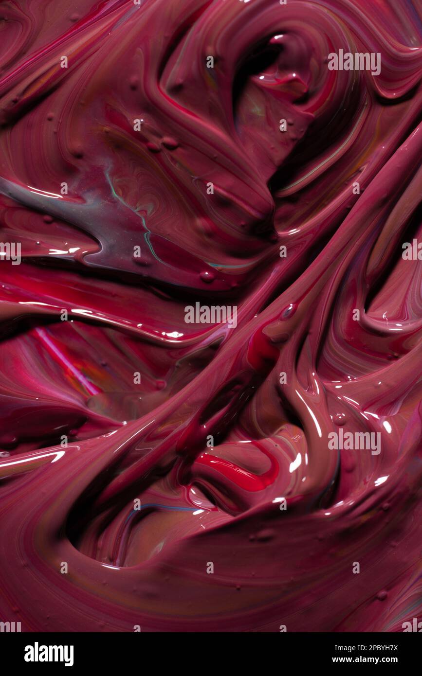 Closeup shot of swirls on surface of thick paint mixing to dark red ...