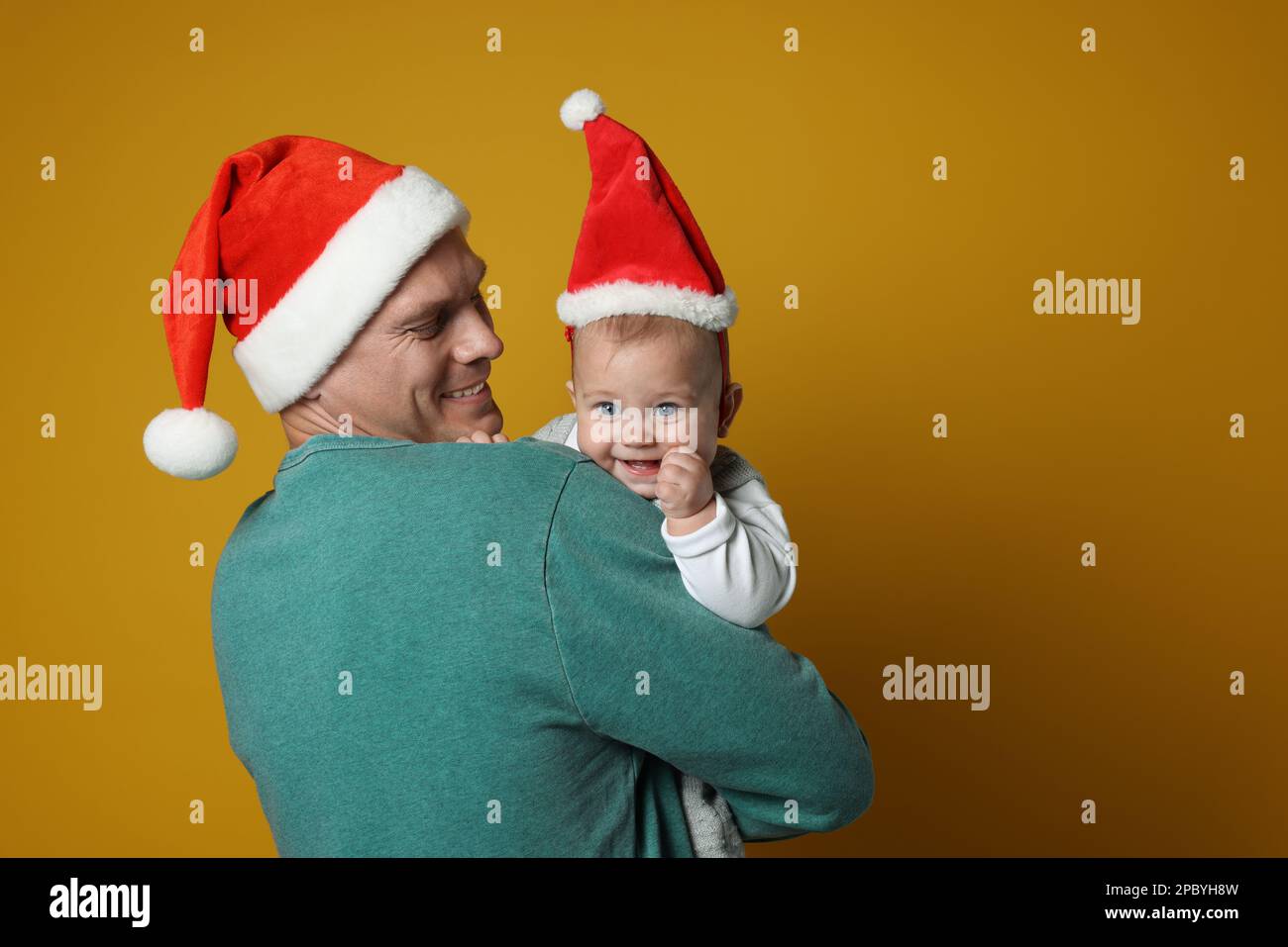 Happy father with cute baby wearing Santa hats on yellow background ...