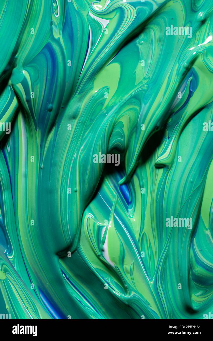 Closeup shot of thick green and blue pigment mixing together into ...