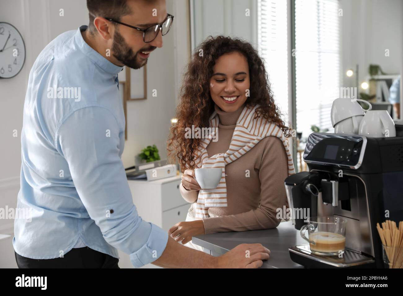 Man talking with colleague while using modern coffee machine in office ...
