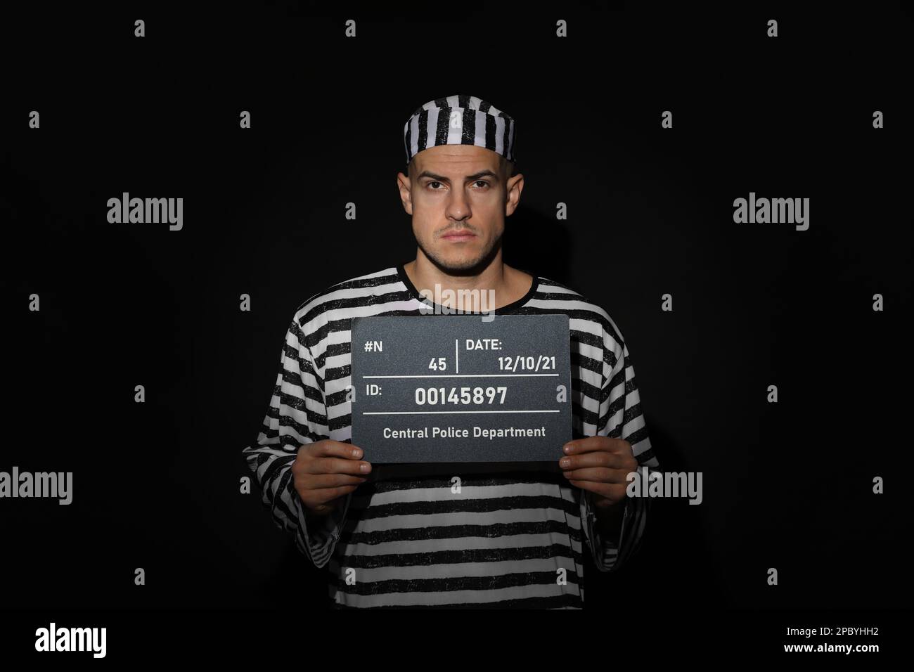 Mug shot of prisoner in striped uniform with board on black background ...