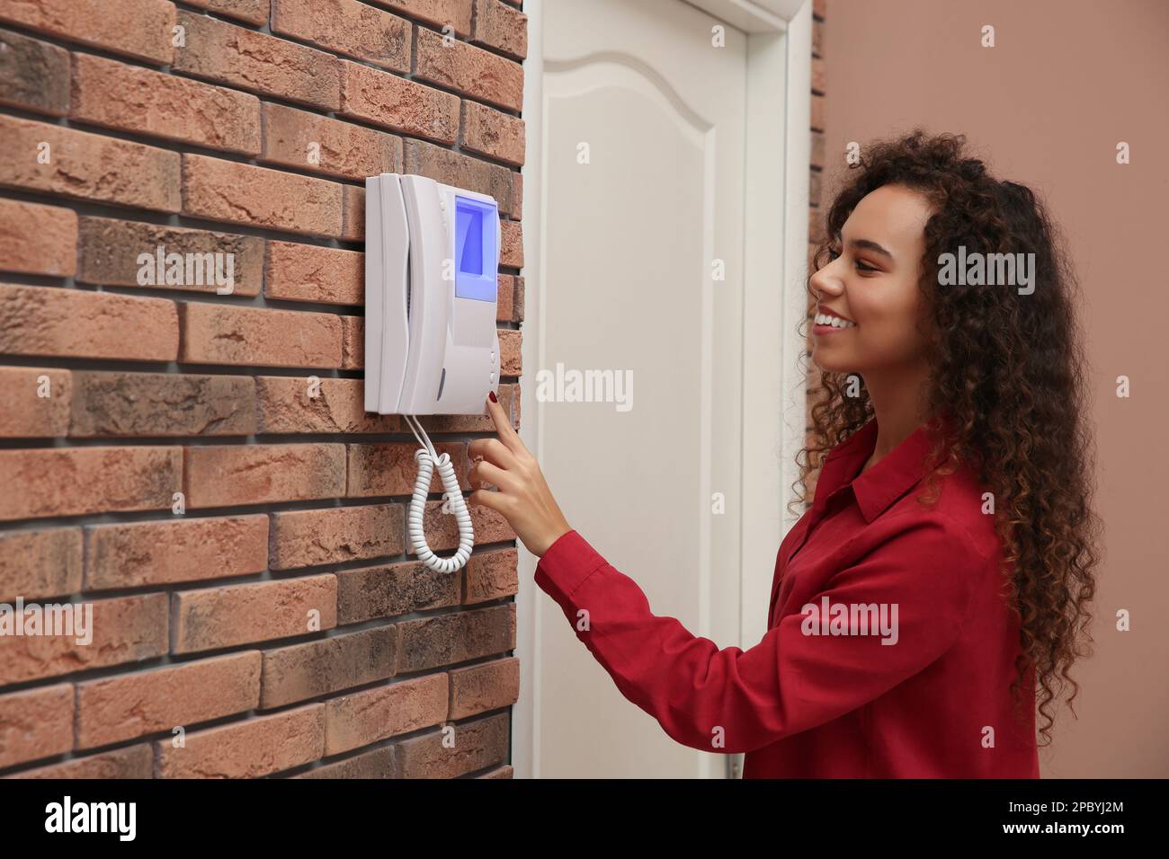 Young African-American woman pressing button on intercom panel indoors ...