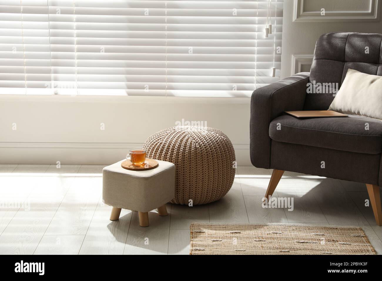 Tray with cup of tea on stylish ottoman and comfortable pouf in room ...