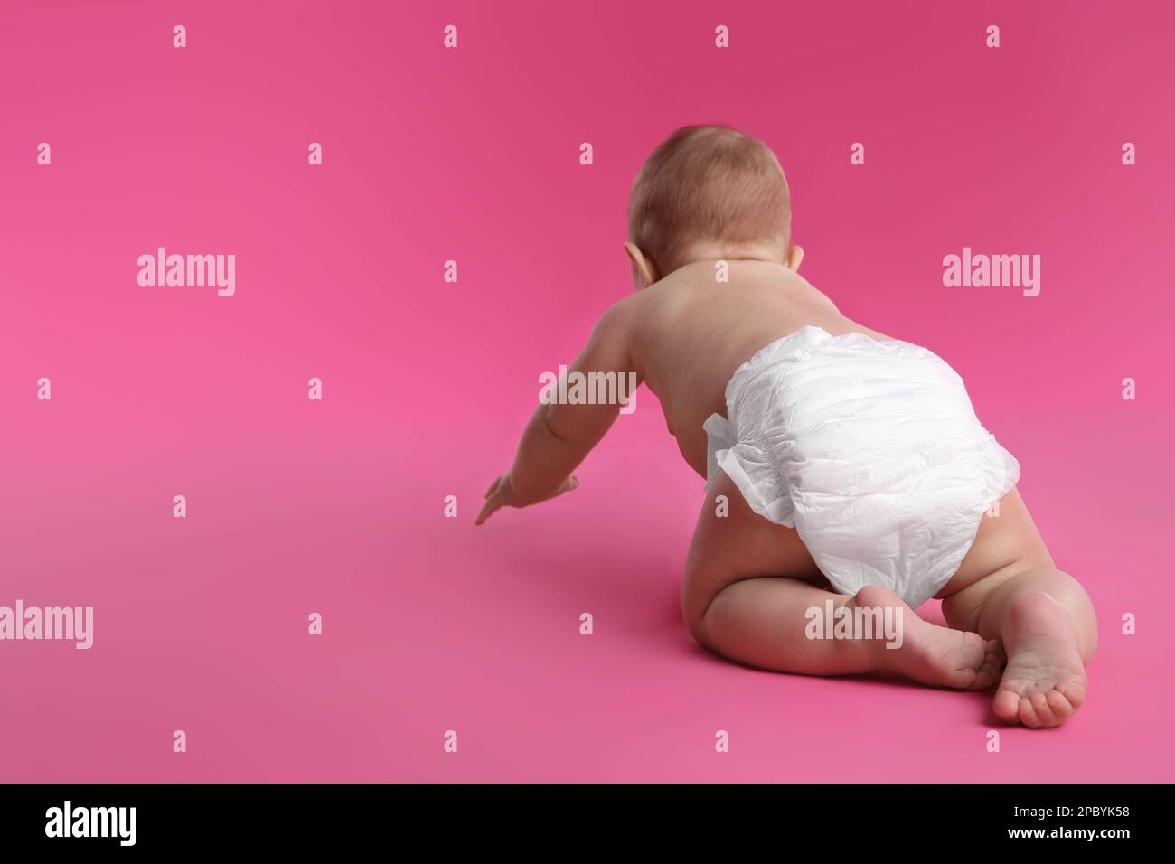 Cute baby in dry soft diaper crawling on pink background, back view ...
