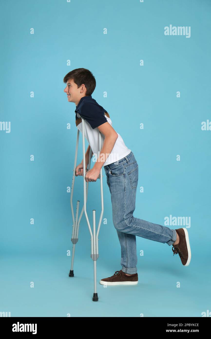 Teenage boy with injured leg using crutches on turquoise background ...