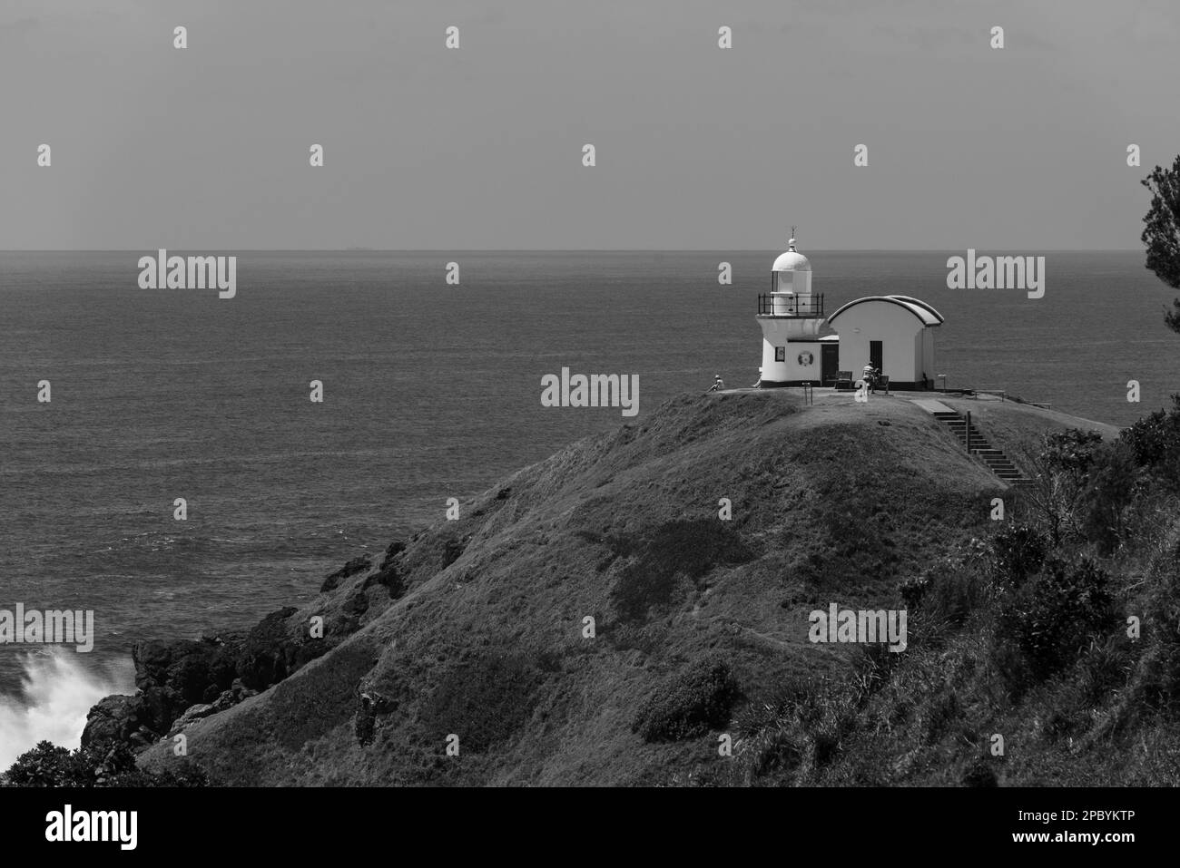 An aerial view of a hillside at the shore with a white lighthouse atop ...