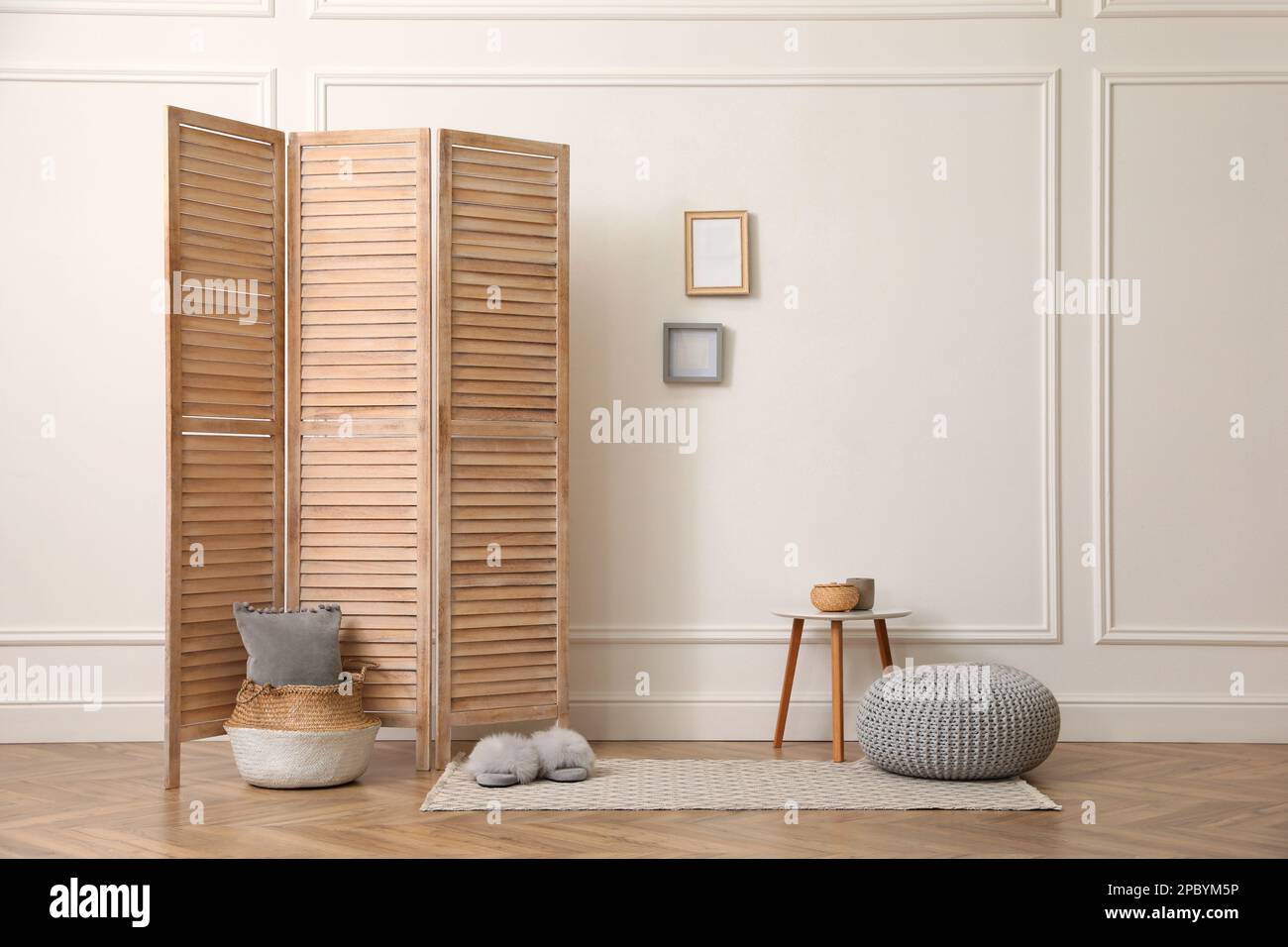 Folding screen, small table and knitted pouf near white wall in room ...