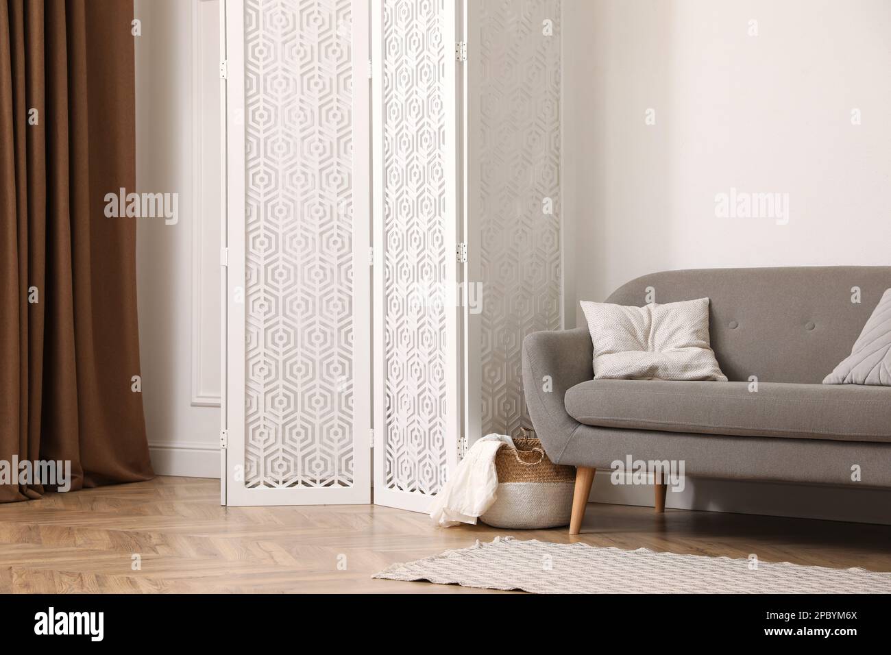 Stylish room with folding screen and sofa near white wall. Interior ...