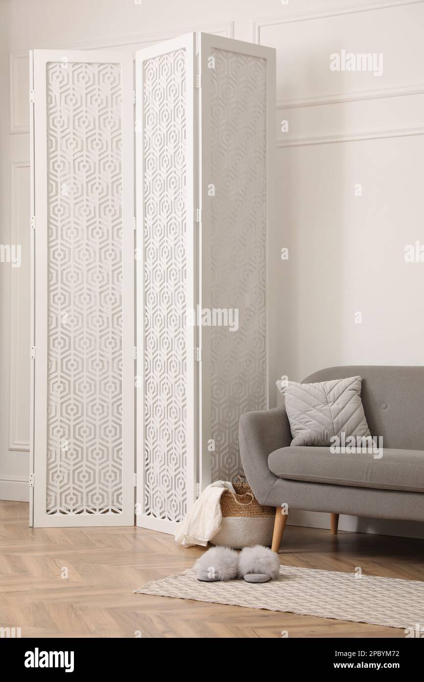 Stylish room with folding screen and sofa near white wall. Interior ...