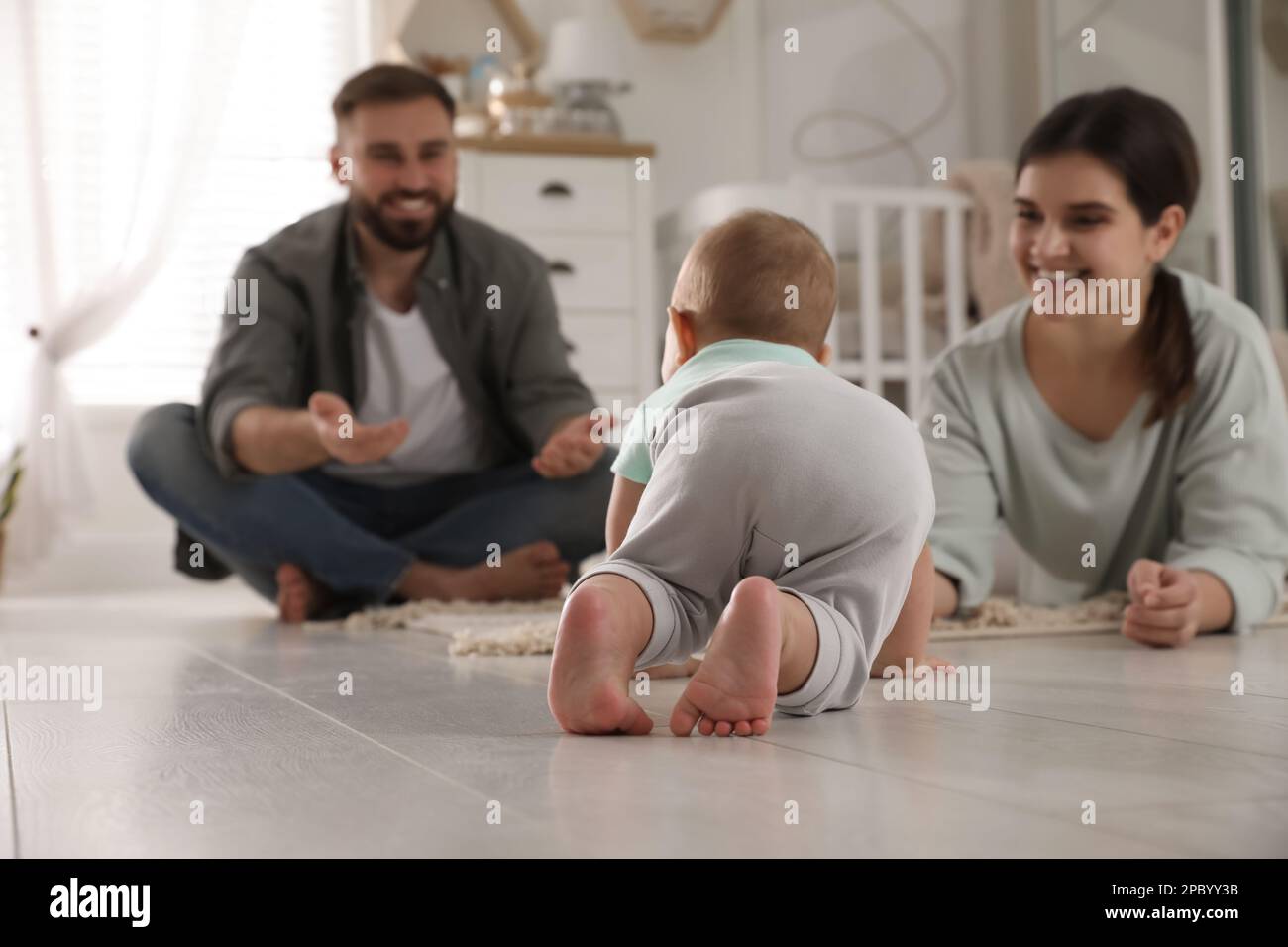 Happy parents watching their baby crawl on floor at home Stock Photo ...