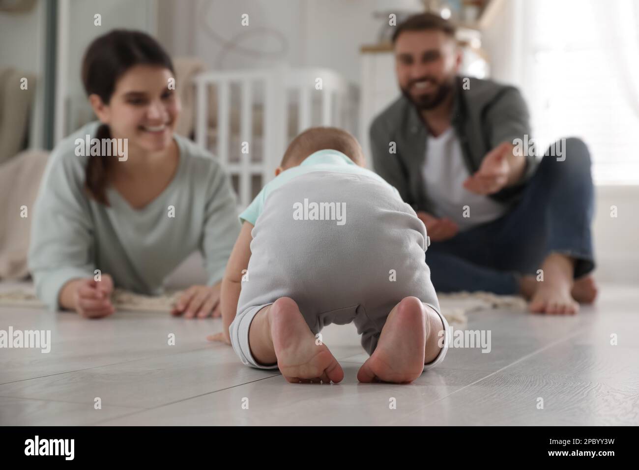 Happy parents watching their baby crawl on floor at home Stock Photo ...
