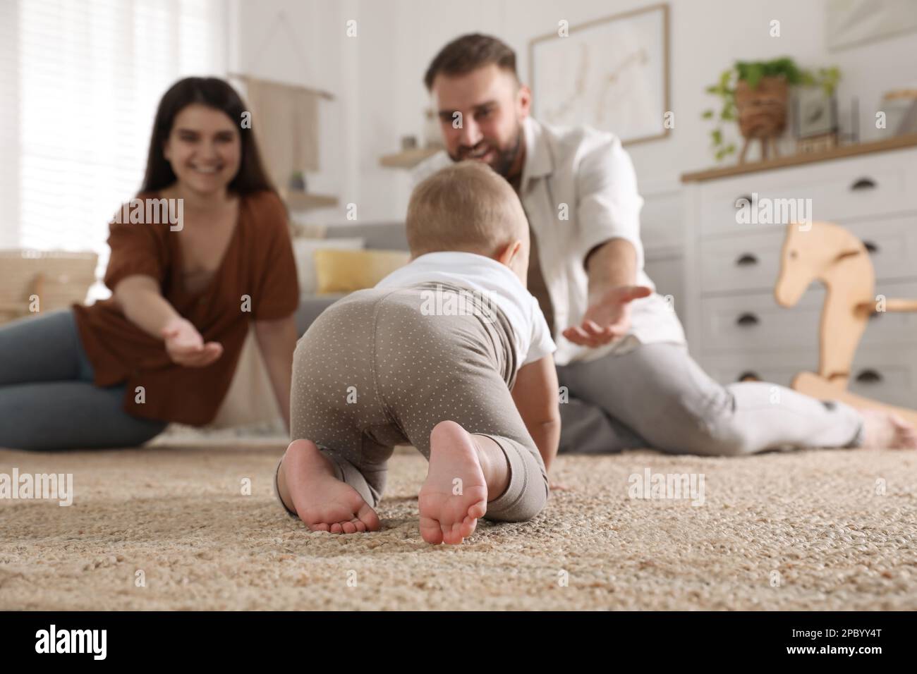 Happy parents watching their baby crawl on floor at home Stock Photo ...