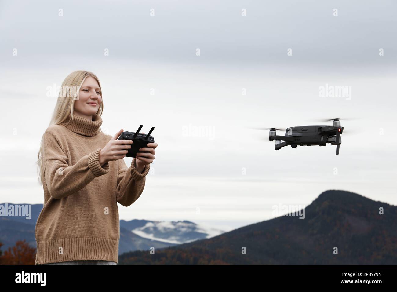 Young woman operating modern drone with remote control in mountains ...