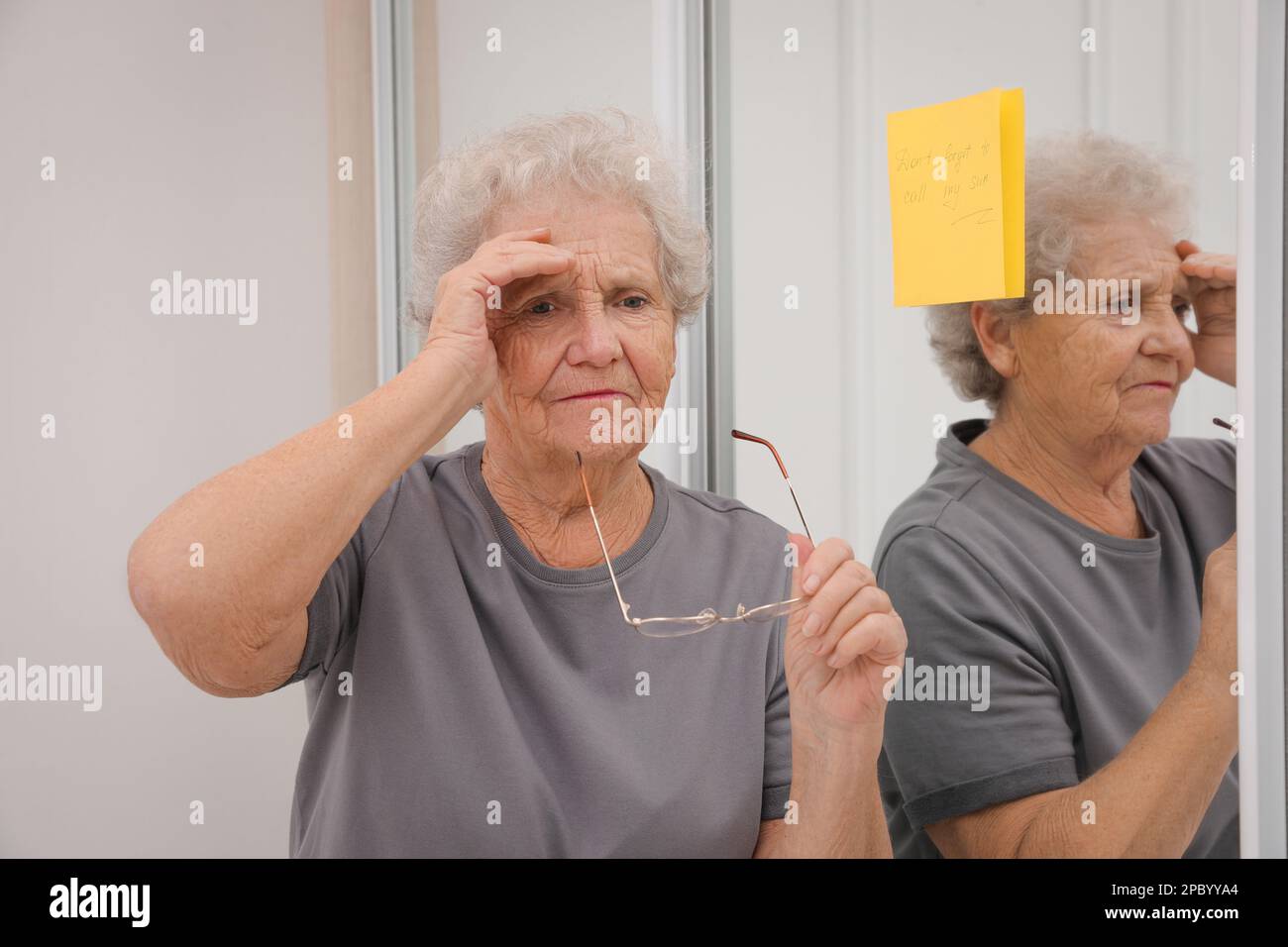 Forgetful senior woman near mirror with reminder note indoors. Age ...