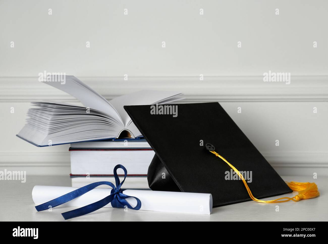 Graduation hat, books and diploma on floor near white wall Stock Photo ...
