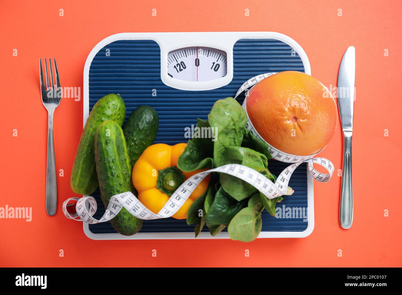 Scales, healthy food, measuring tape and cutlery on orange background ...