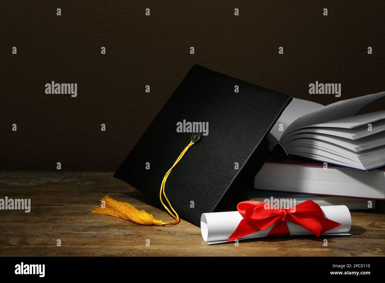 Graduation hat, books and diploma on wooden table against brown ...