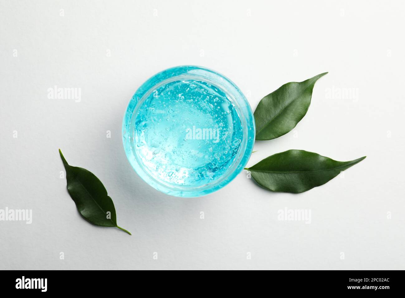 Jar of blue cosmetic gel and green leaves on white background, flat lay ...