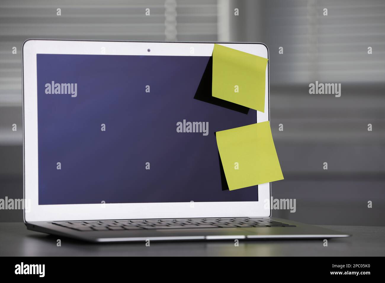 Laptop with blank sticky notes on grey office desk. Space for text ...