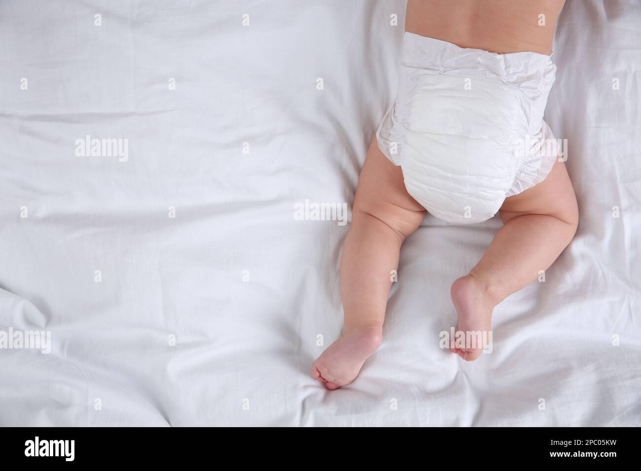 Top view of cute baby in dry soft diaper on white bed. Space for text ...
