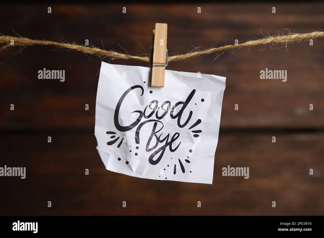 Crumpled paper note with word Goodbye hanging on twine against wooden ...
