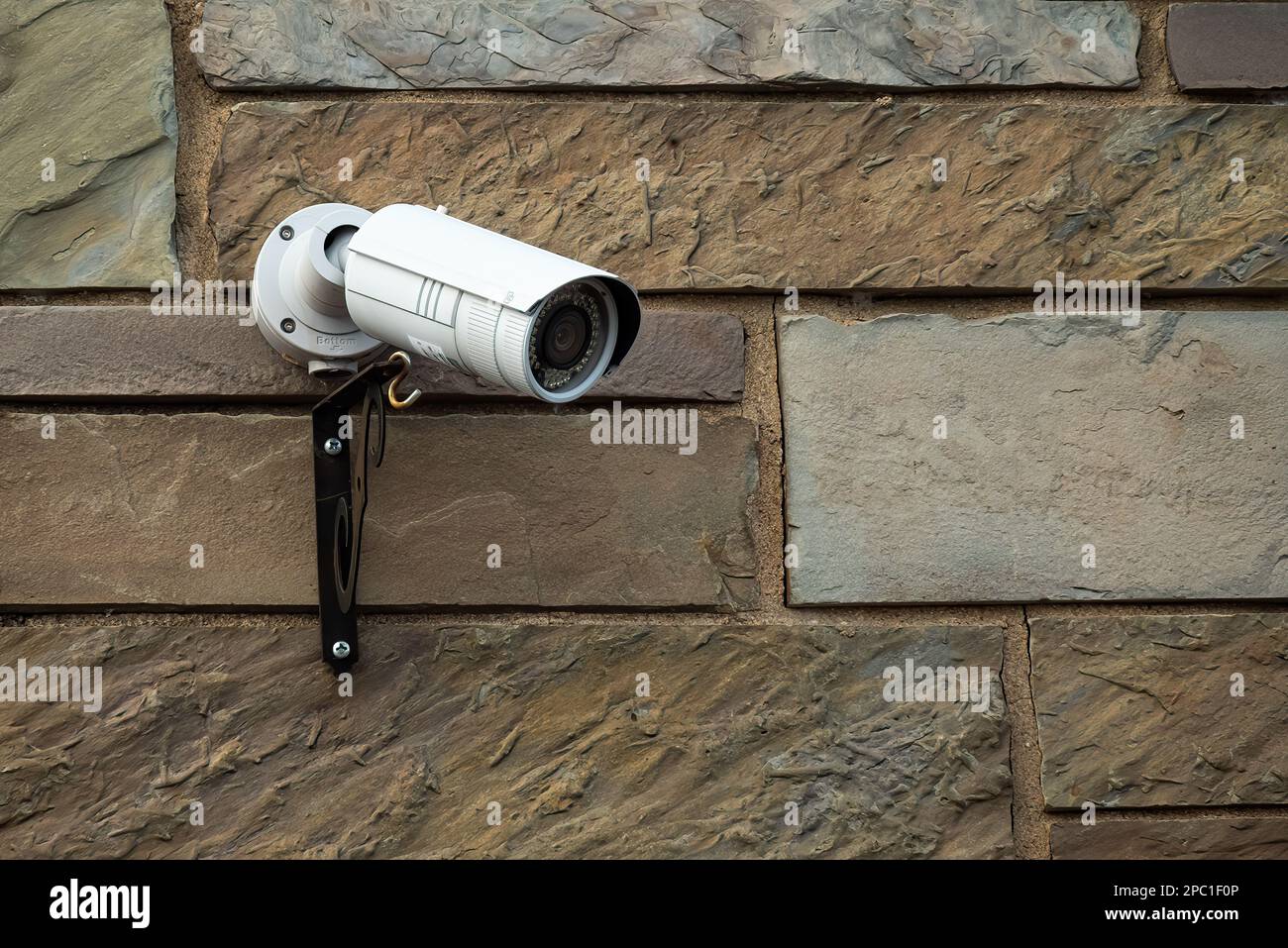 A white video surveillance camera mounted high on a rock faced exterior ...