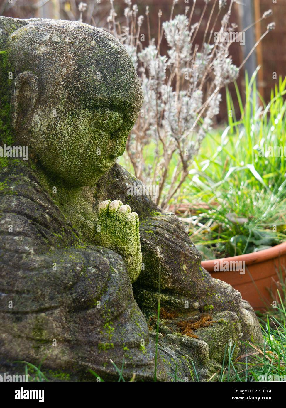 Monk statue made of stone prays in the sunshine in the green grass ...