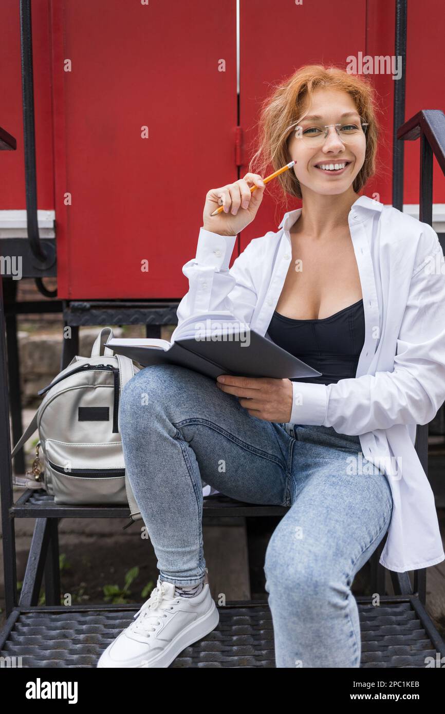 Young attractive woman sitting at the stairs and drawing sketch in the ...