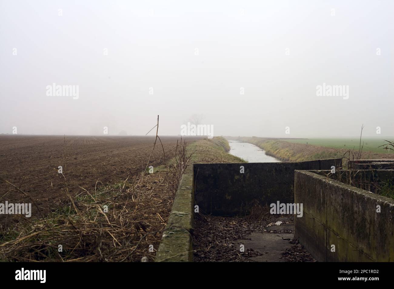 Dry irrigation channel and a stream of water between field on a foggy ...
