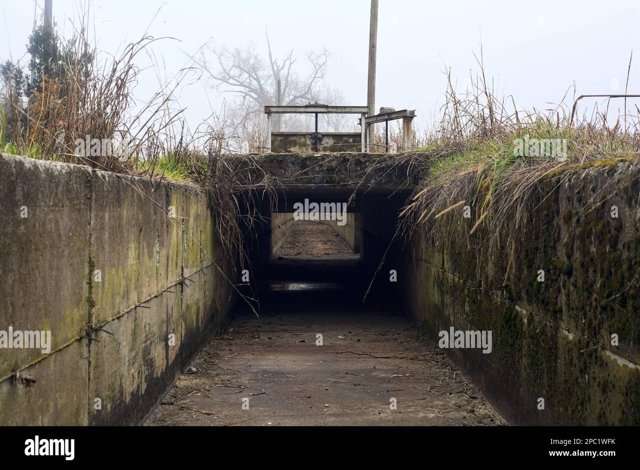 Dry irrigation channel and a rusty weir on a foggy day in the italian ...