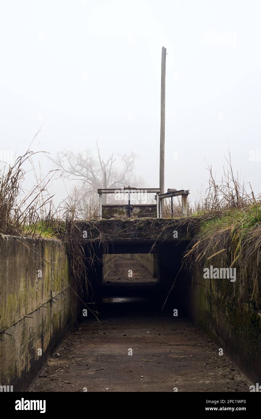 Dry irrigation channel and a rusty weir on a foggy day in the italian ...