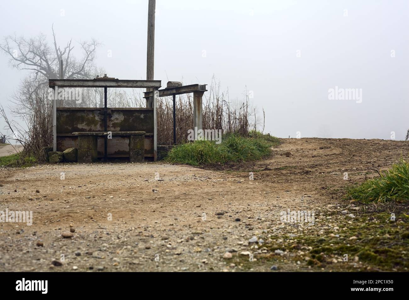 Dry irrigation channel and a rusty weir on a foggy day in the italian ...