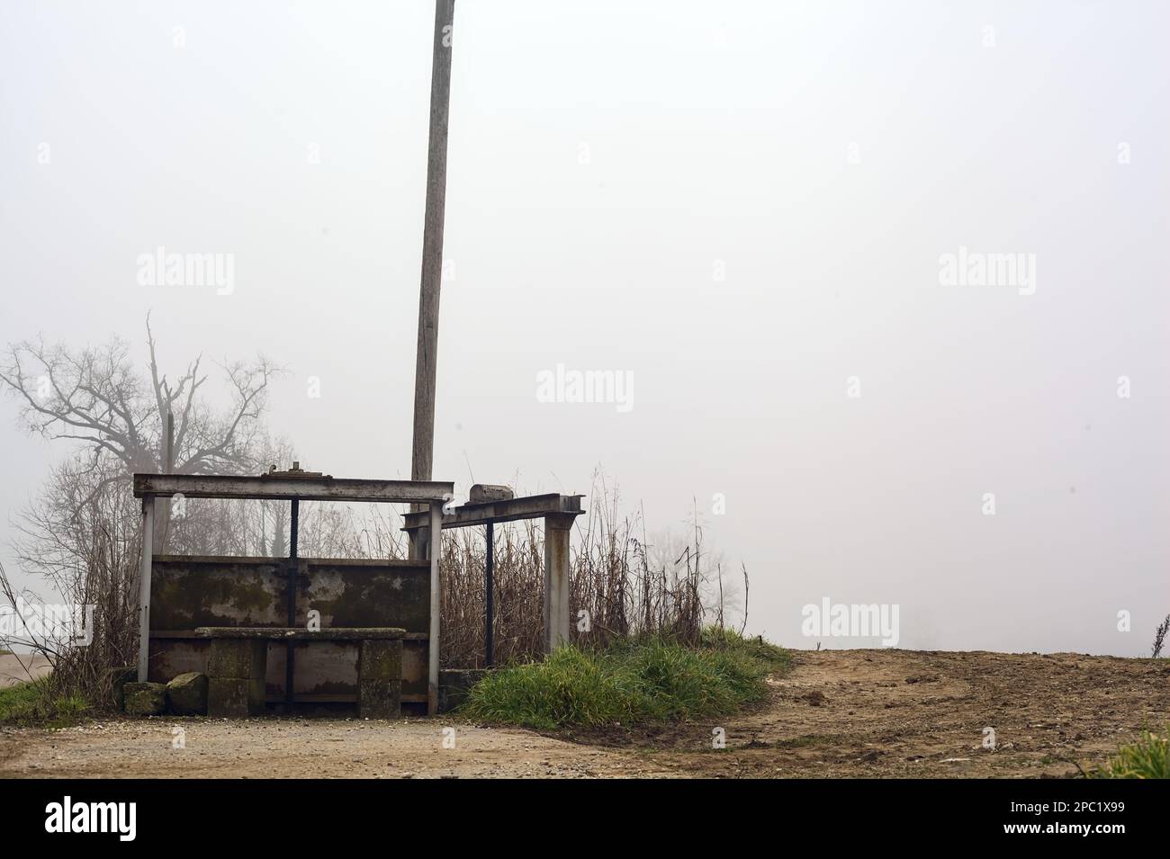 Dry irrigation channel and a rusty weir on a foggy day in the italian ...