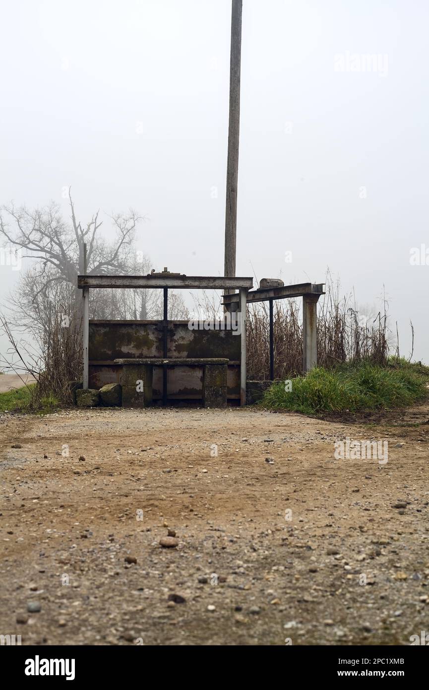 Dry irrigation channel and a rusty weir on a foggy day in the italian ...