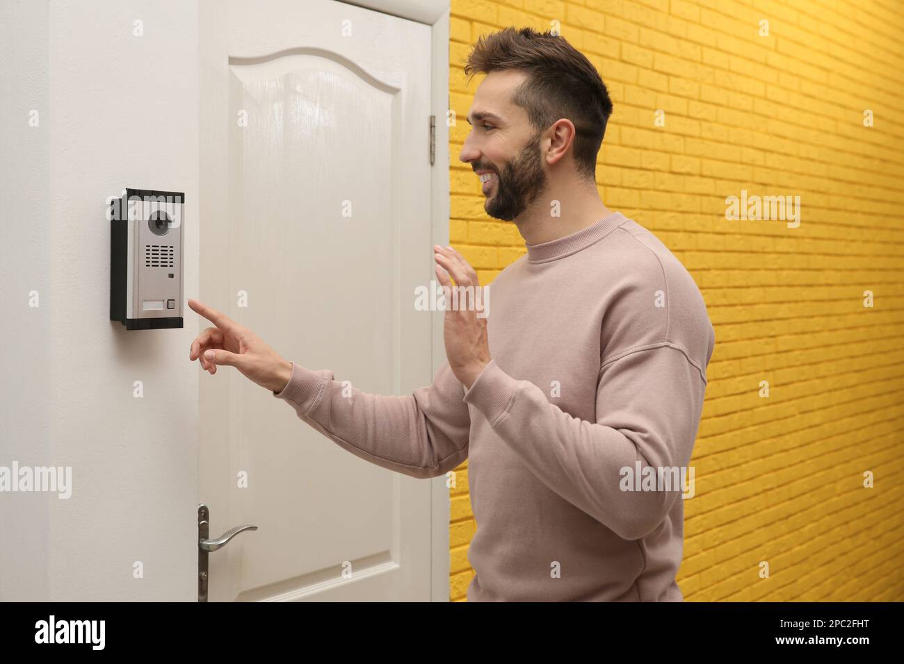 Happy man ringing intercom while waving to camera in entryway Stock ...