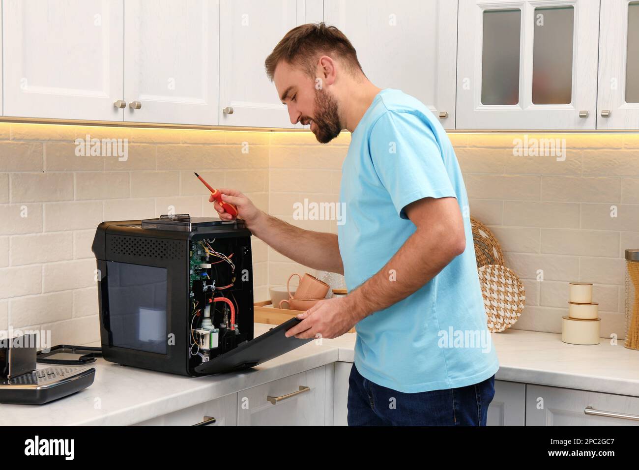 Man with screwdriver fixing coffee machine at table in kitchen Stock ...