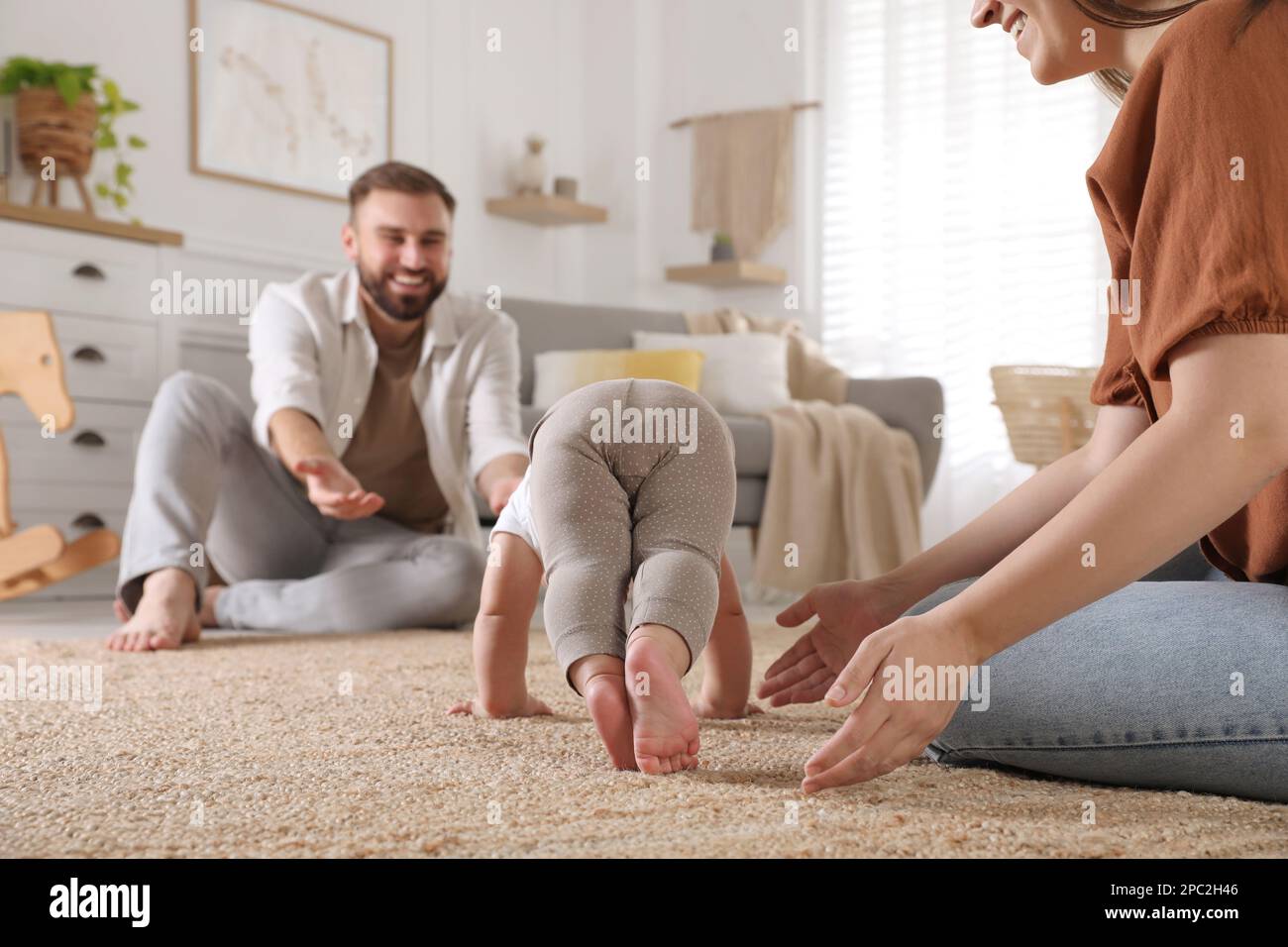 Happy parents watching their baby crawl on floor at home Stock Photo ...