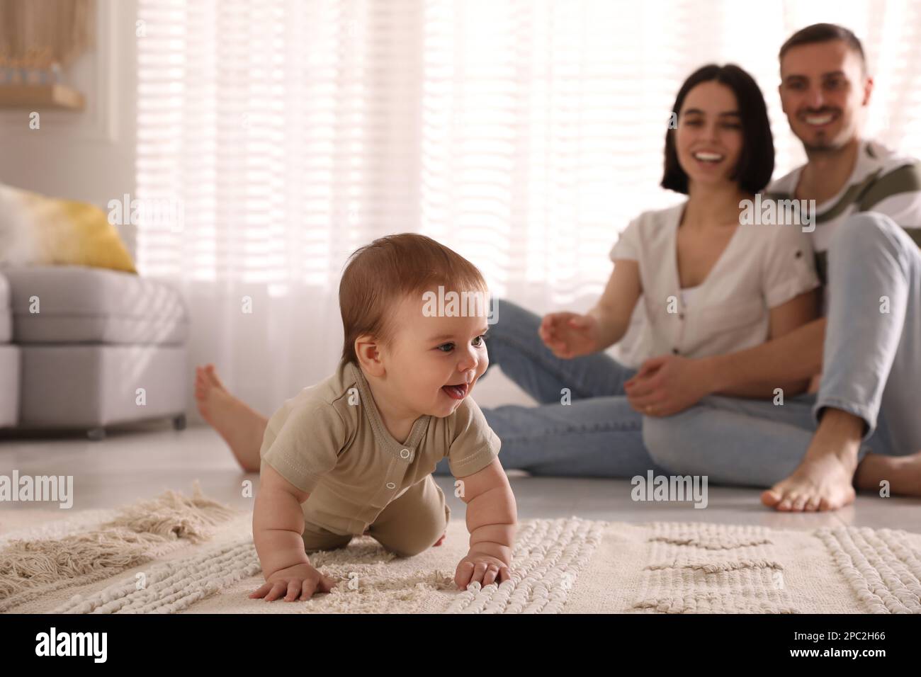 Happy parents watching their cute baby crawl on floor at home Stock ...