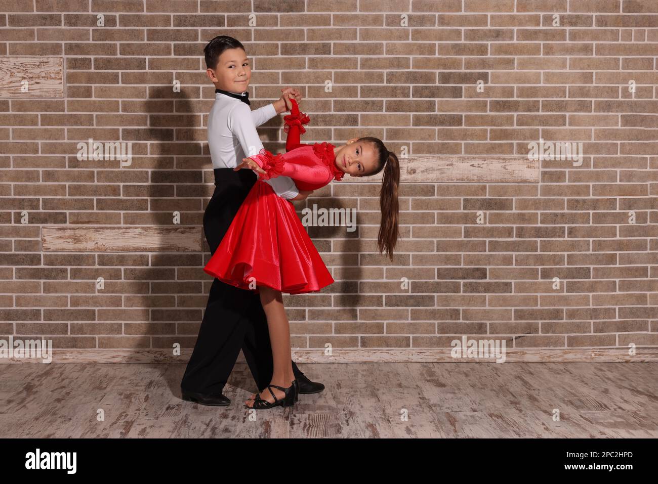 Beautifully dressed couple of kids dancing together near brick wall ...
