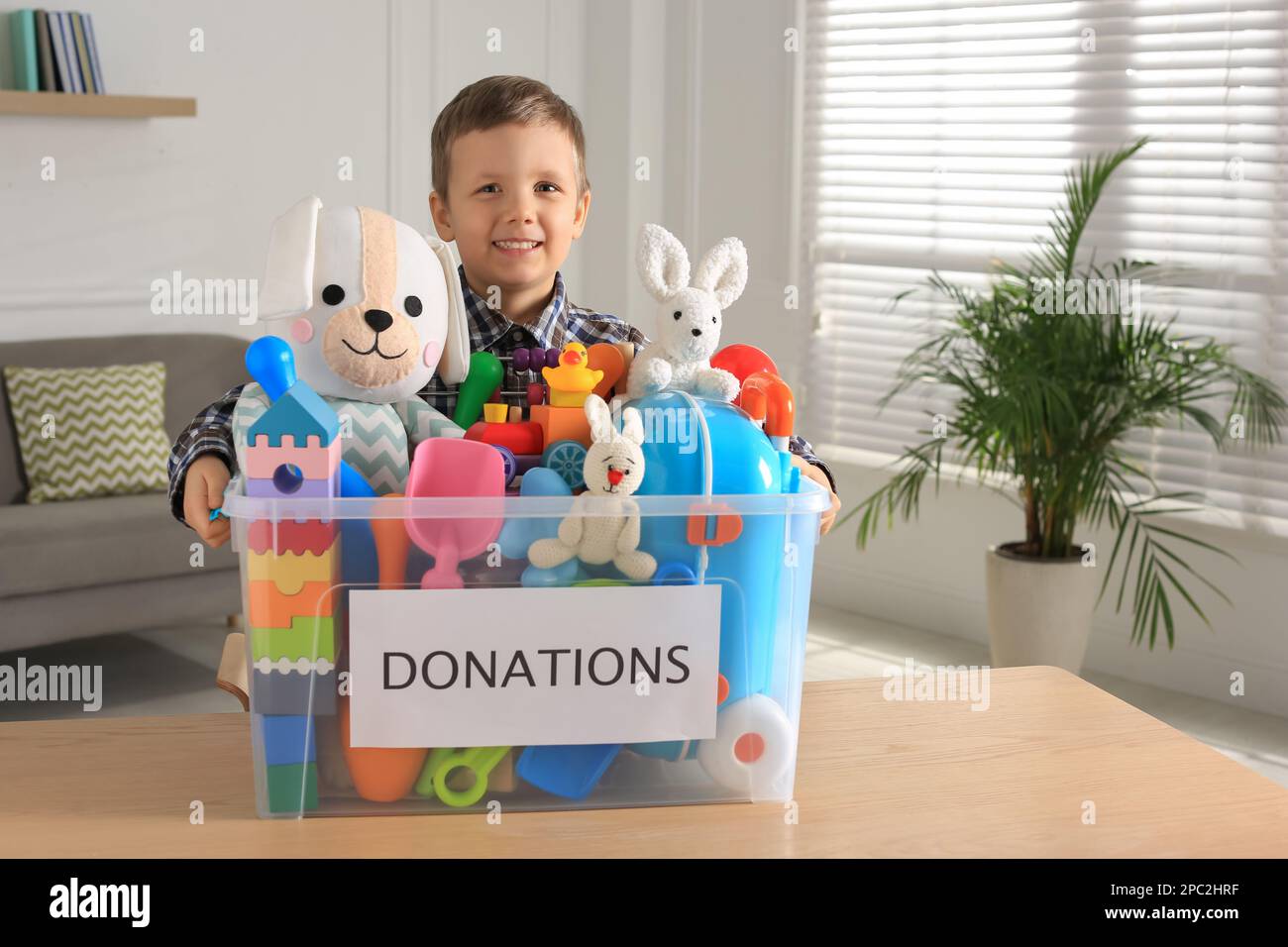 Cute little boy holding donation box with toys at home, space for text ...