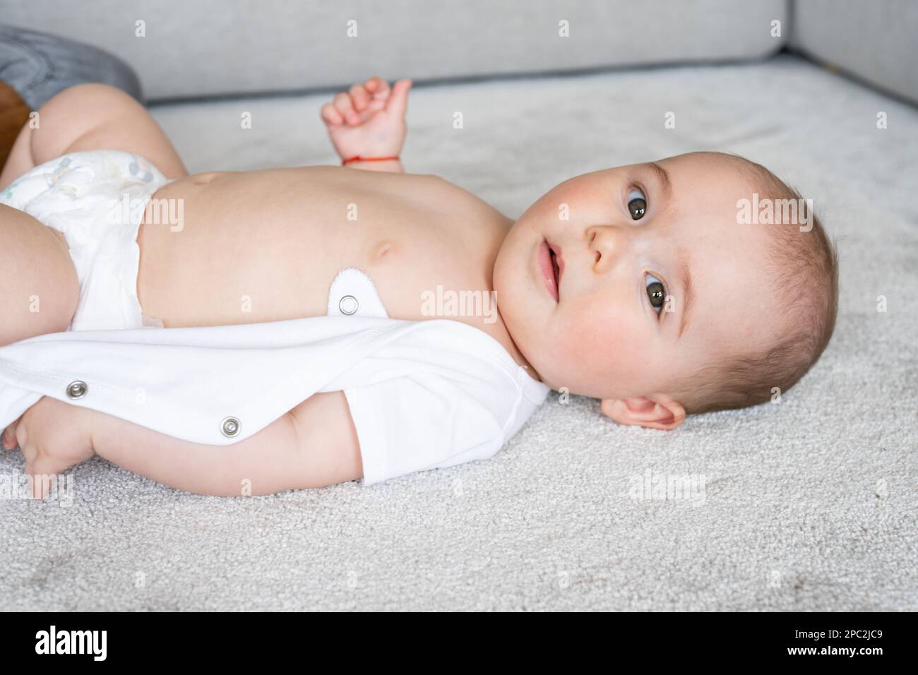 childhood, babyhood and people concept - happy little baby boy or girl lying on floor at home ...