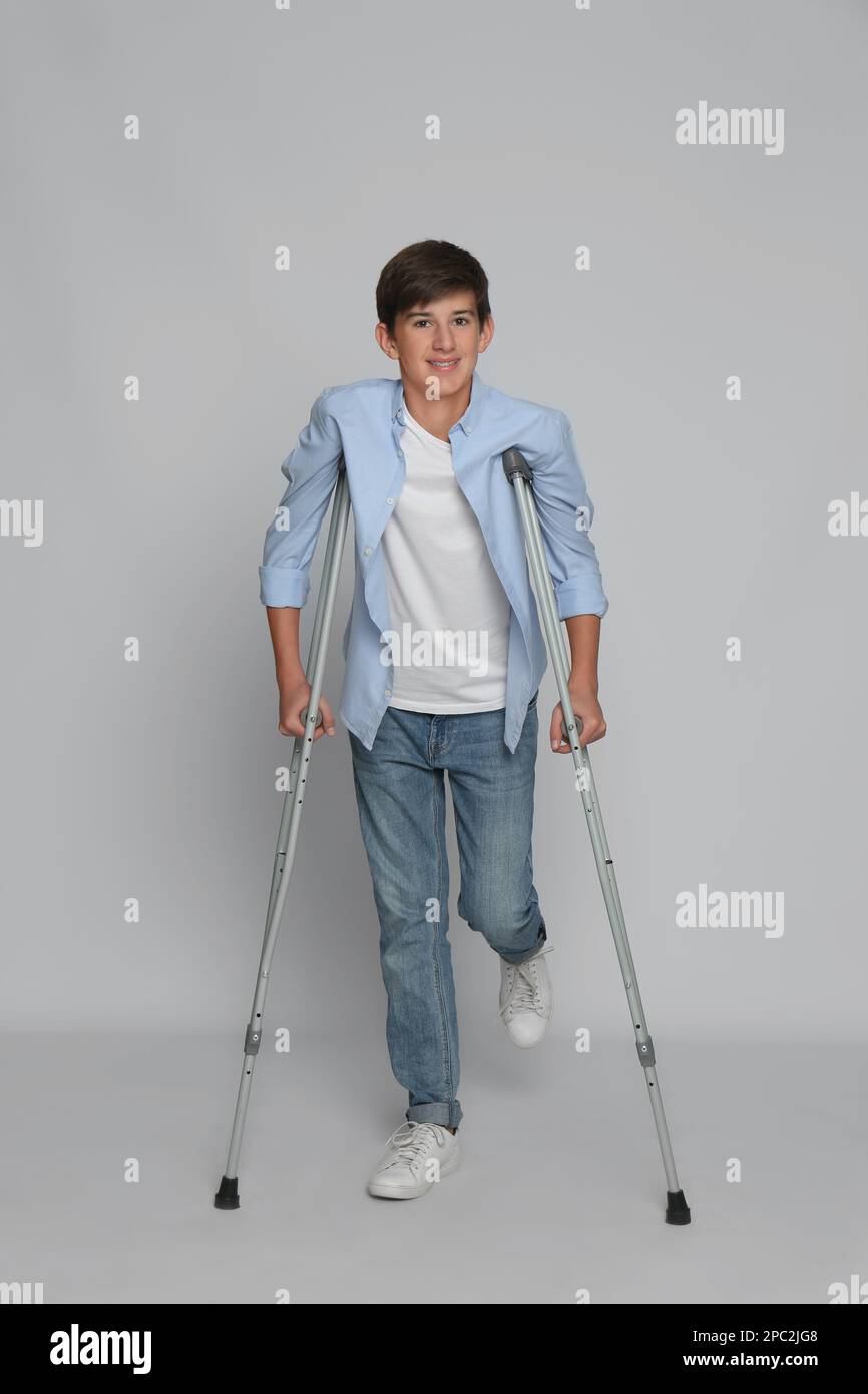 Teenage boy with injured leg using crutches on grey background Stock ...
